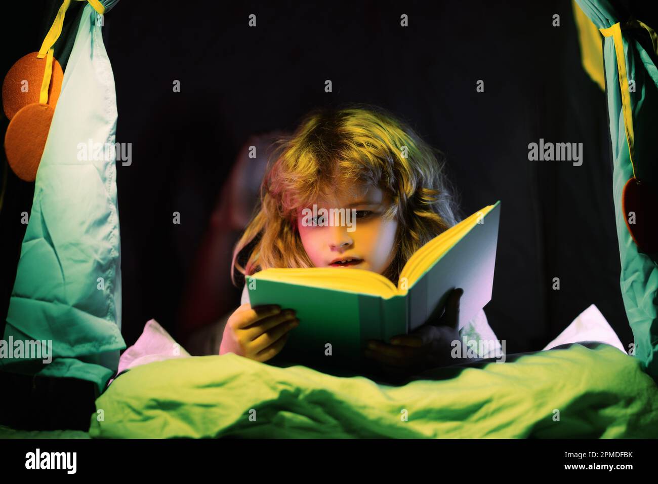 Kid boy in kids tent reading books. Kids face with night light. Concept ...