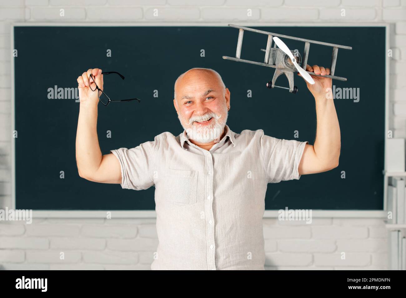 Funny senior teacher in the classroom on blackboard background. Old fun ...