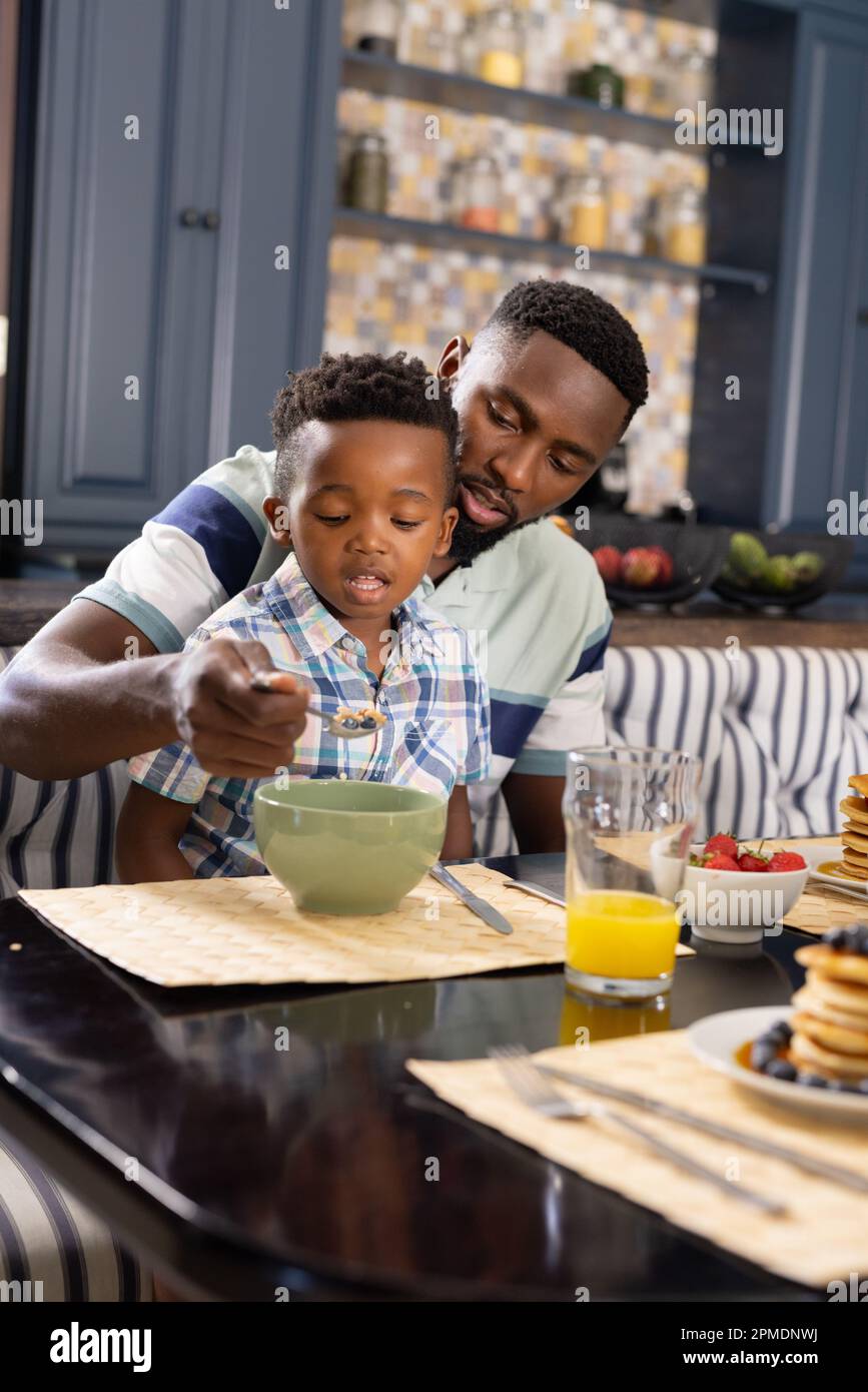 African american father feeding breakfast cereals to son at dining ...