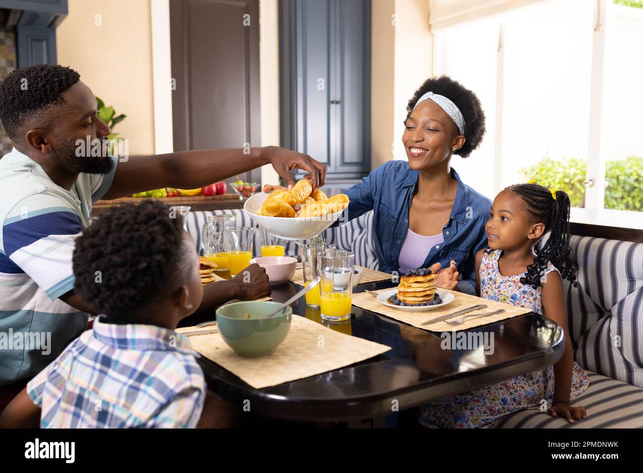 African american woman sharing croissant with husband while having breakfast with children at ...