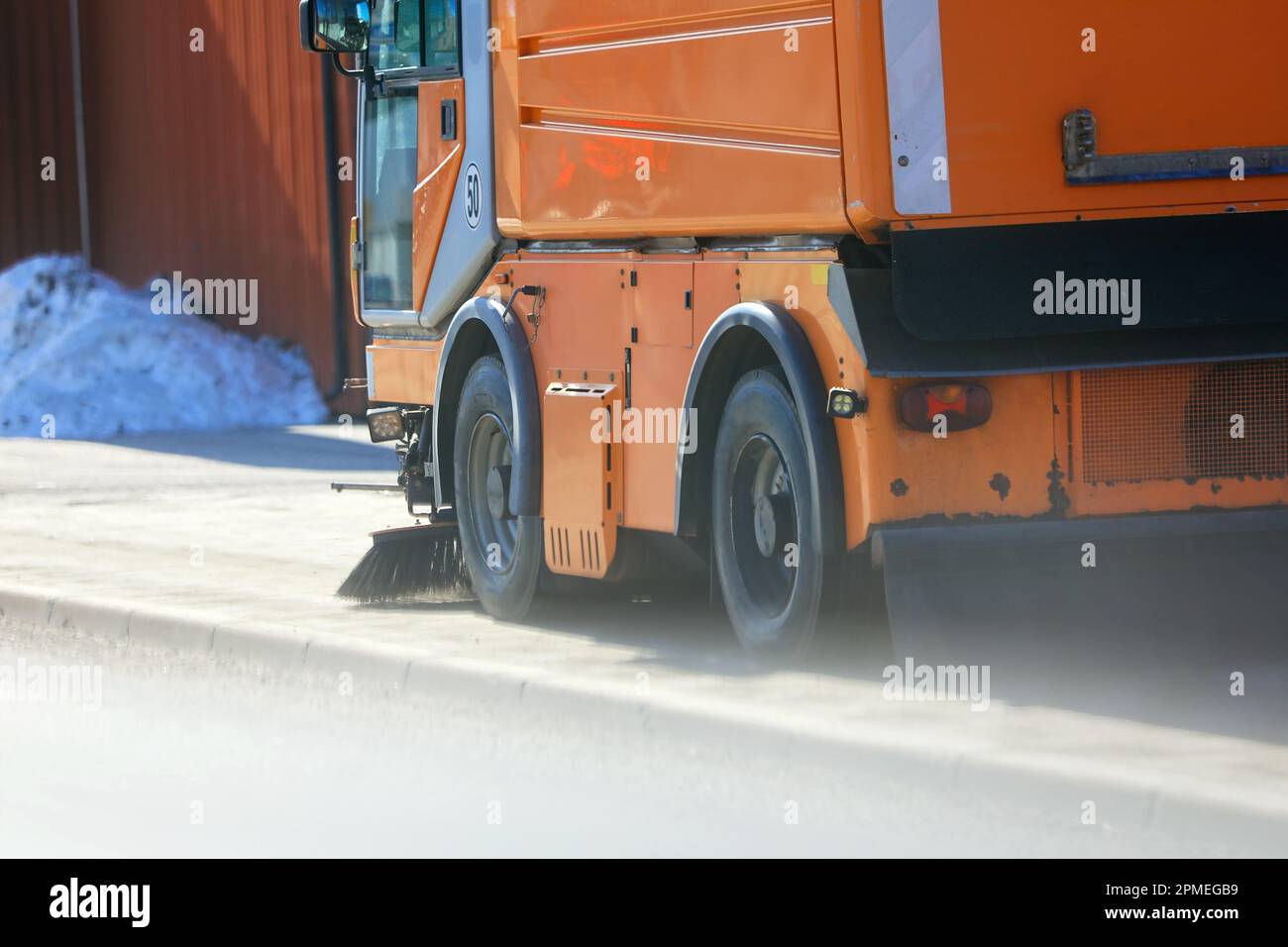 Orange street sweeper machine cleaning the pavement on a day of spring ...