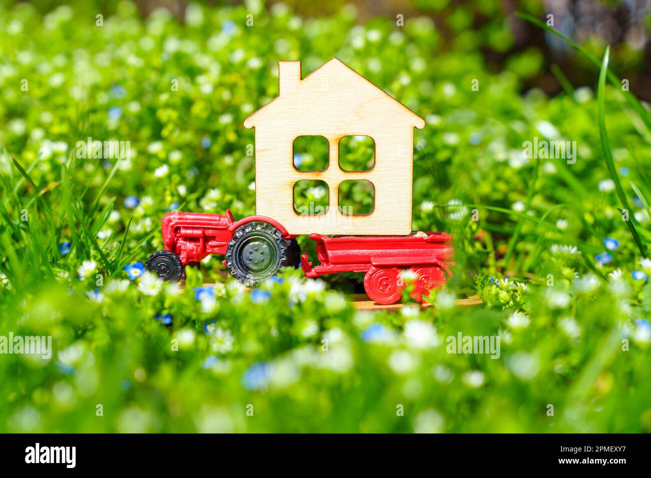 Miniature tractor carrying a flat house model placed on a flowerbed of ...