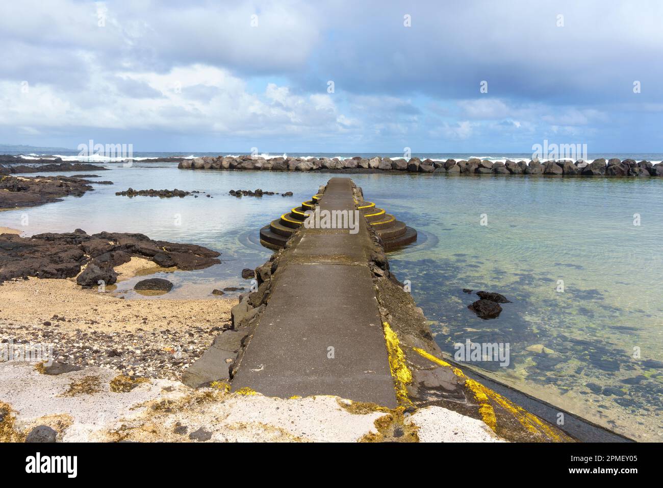 Serene Hawaii beach with a shallow swimming area and a stone pier with ...
