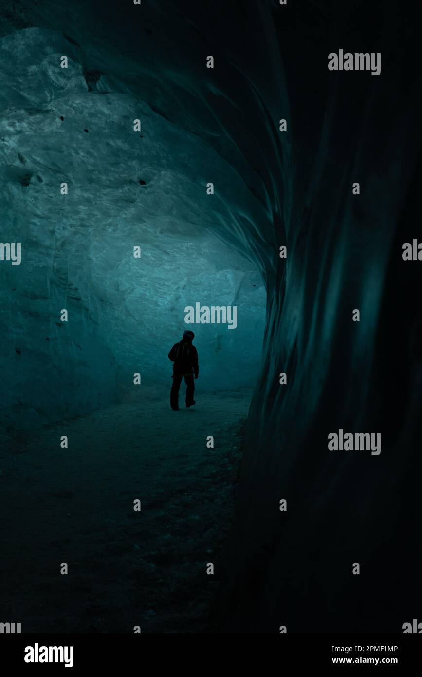 A man stands in an awe-inspiring and mysterious dark ice cave ...