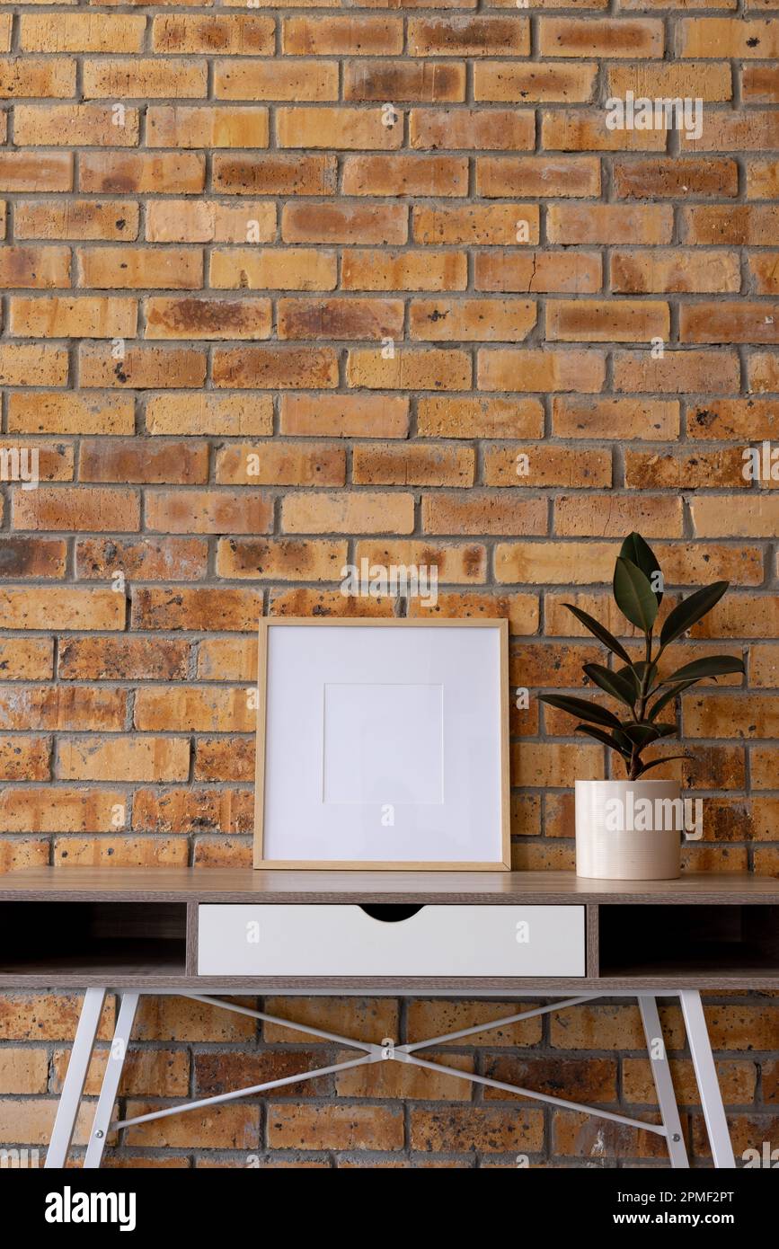 Vertical of empty wooden frame with copy space and plant in pot on desk ...
