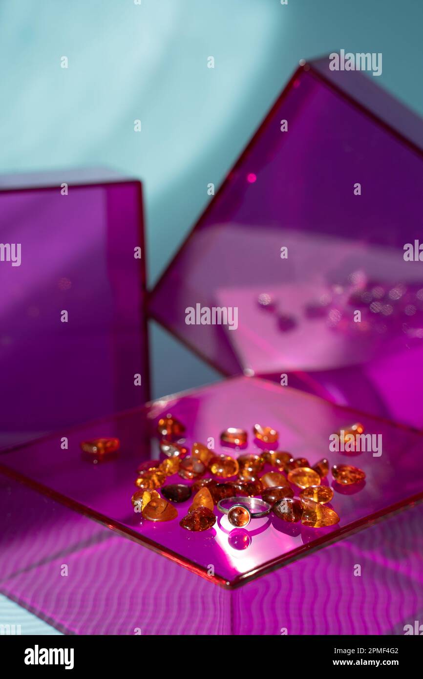 Amber ring and stones on pink glass podium and blue sunlit background ...