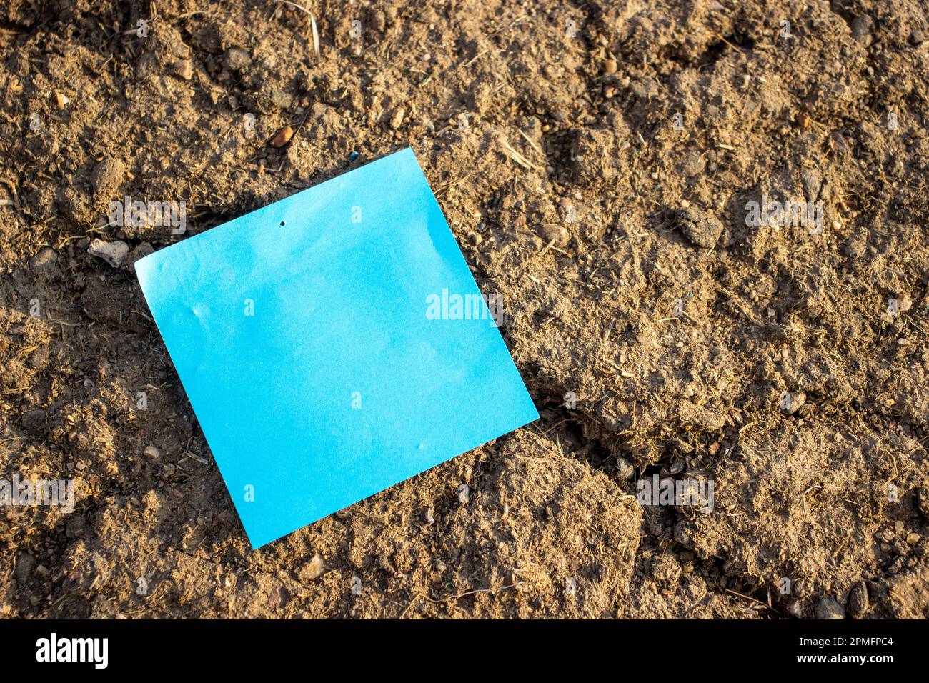 single blue square paper note laying on dried brown earth with empty ...
