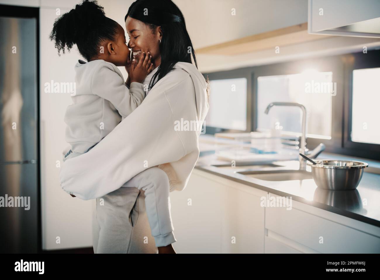 Daughter kisses her mom on the mouth as she sits in her arms on mother ...