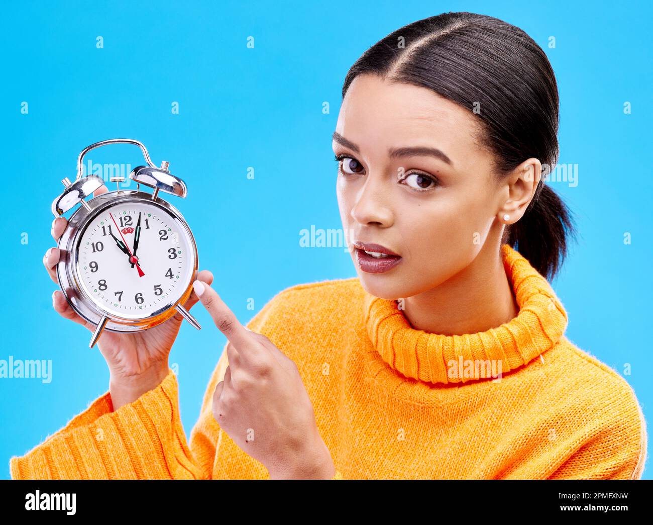 Woman, annoyed and pointing at alarm clock in portrait for warning by ...