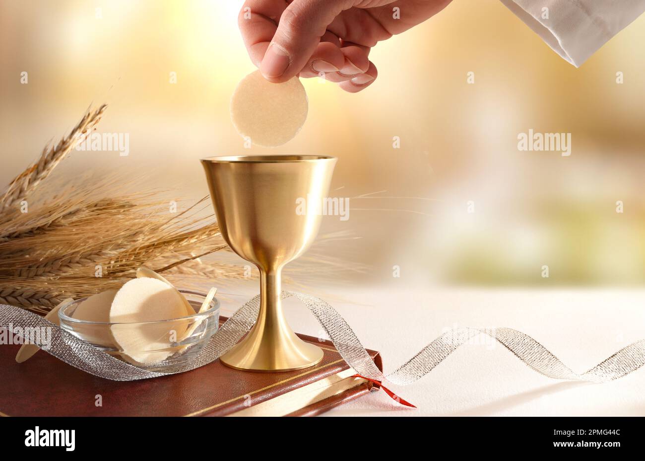 Priest dipping host into wine at Eucharist with glass on bible on white ...