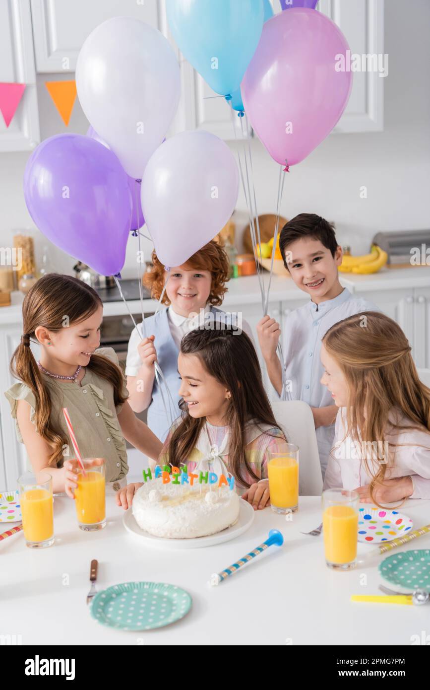 cheerful kids with balloons looking at birthday girl near cake and ...