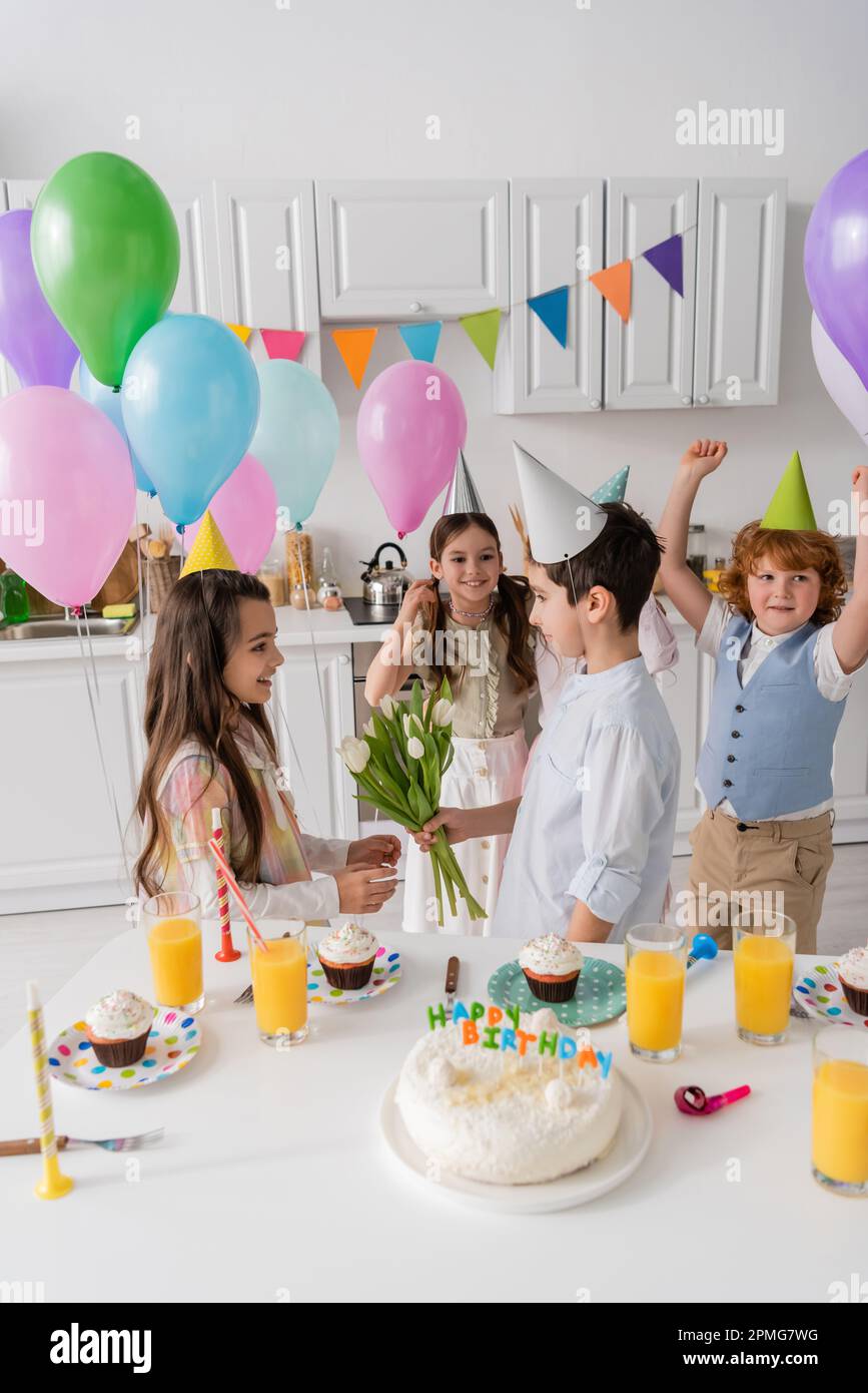 preteen boy giving flowers to cheerful birthday girl near friends on ...