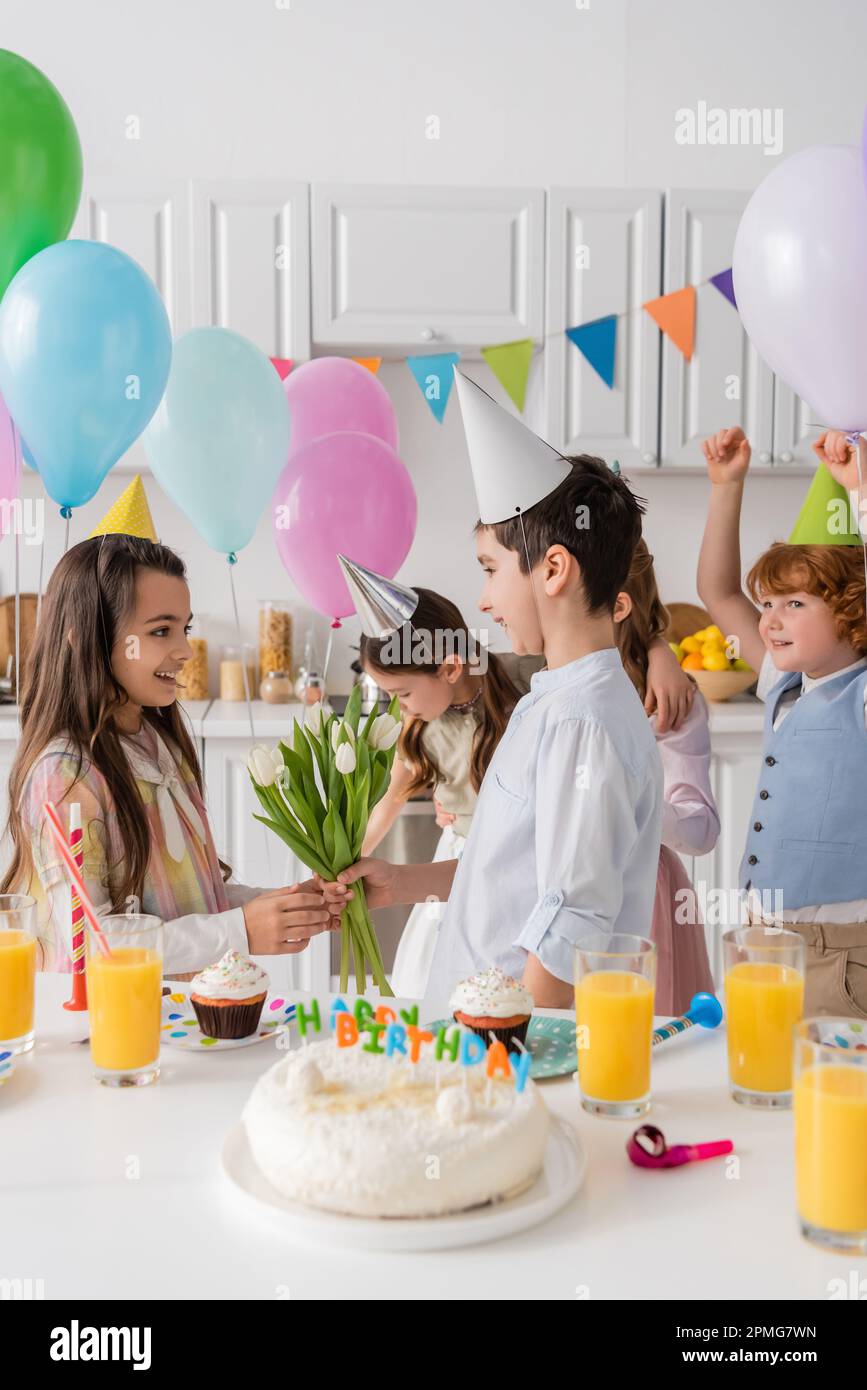 preteen boy giving tulips to happy birthday girl near friends on ...