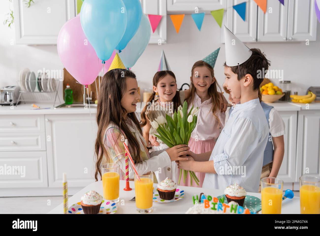 happy preteen boy giving flowers to cheerful birthday girl near friends ...