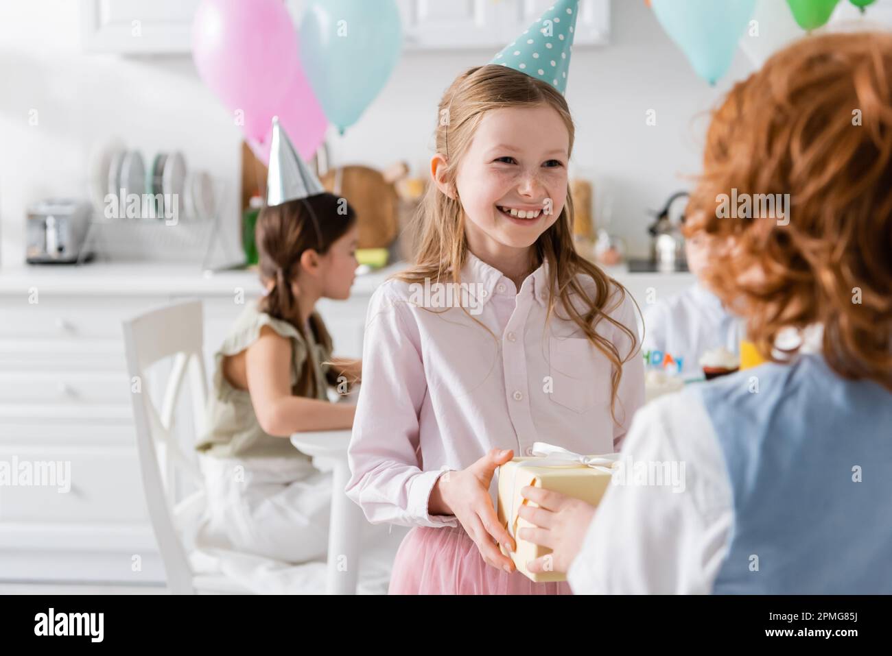 happy girl in cap receiving present from redhead friend during birthday ...