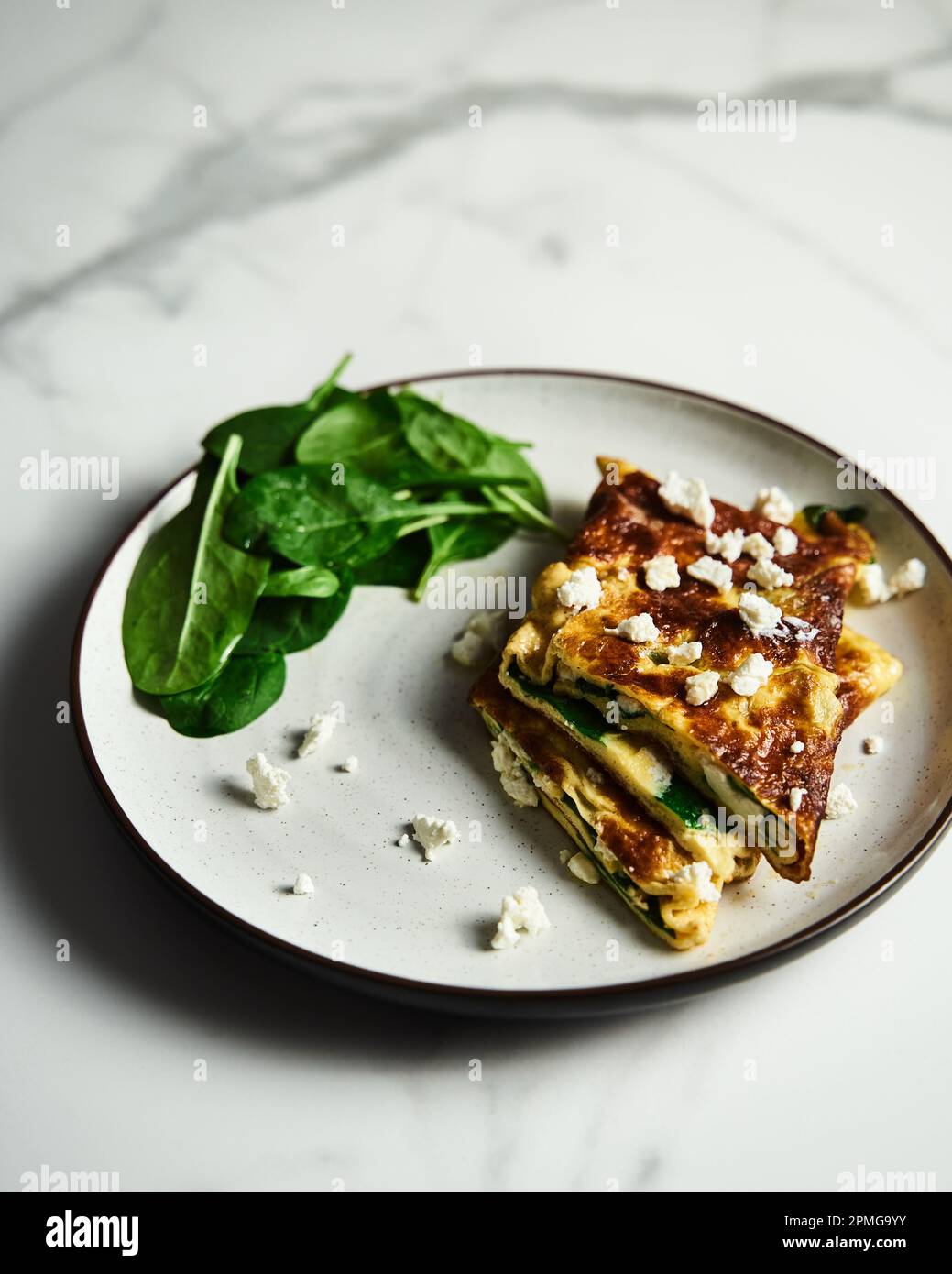 Folded omelette stuffed with spinach and feta on the white plate with ...