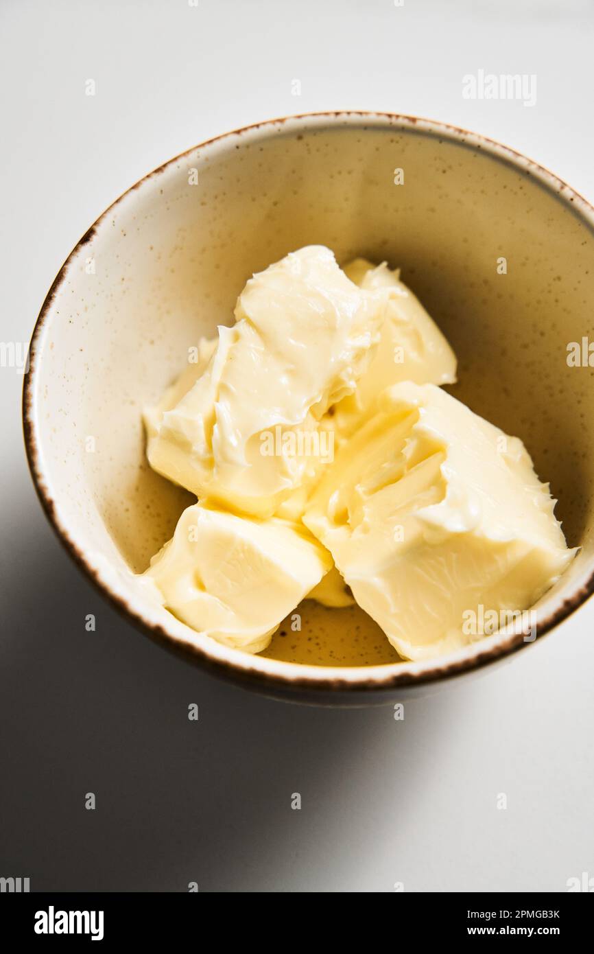 Unsalted butter cubes in white bowl on white marble background. The oil ...