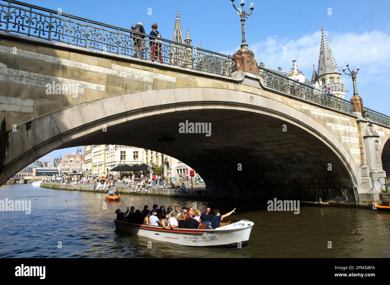 Tourist boat on the Leie river crossing under a bridge with historical ...