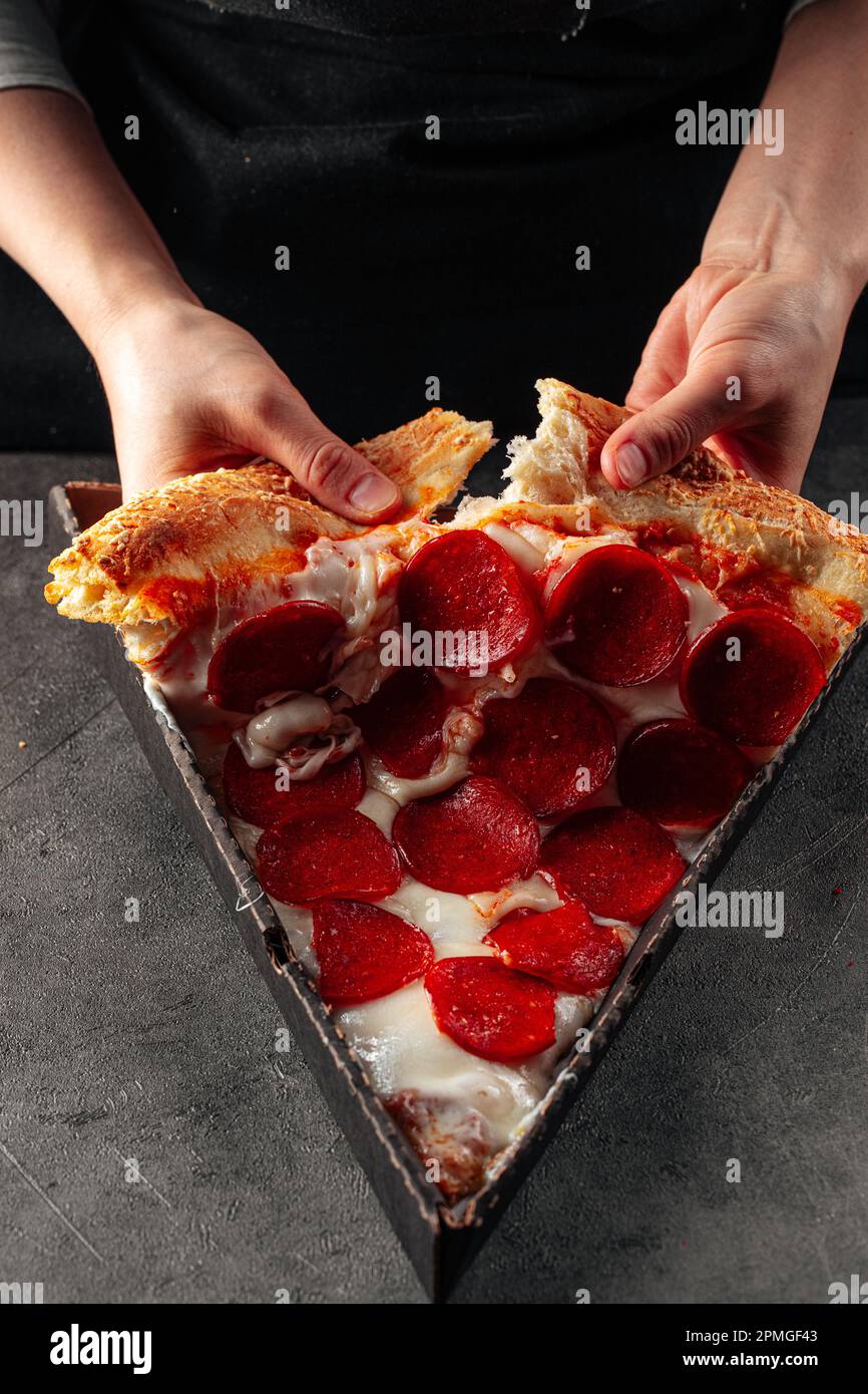 Baker tearing off a slice of pepperoni pizza Stock Photo - Alamy