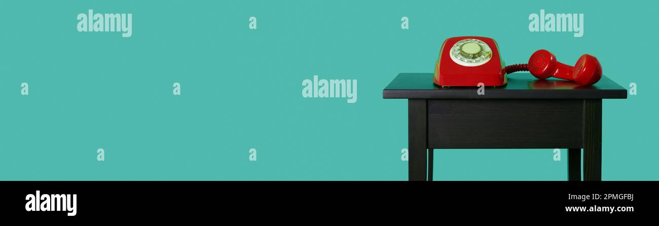 a red landline rotary dial telephone, with its handset off the hook on ...