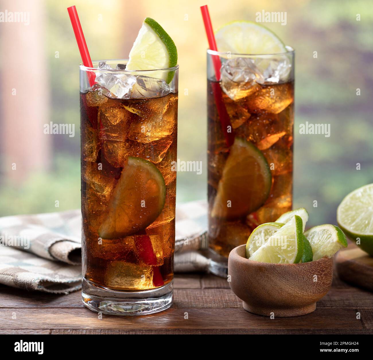 Rum and cola cocktail with lime slice on rustic wooden table with ...