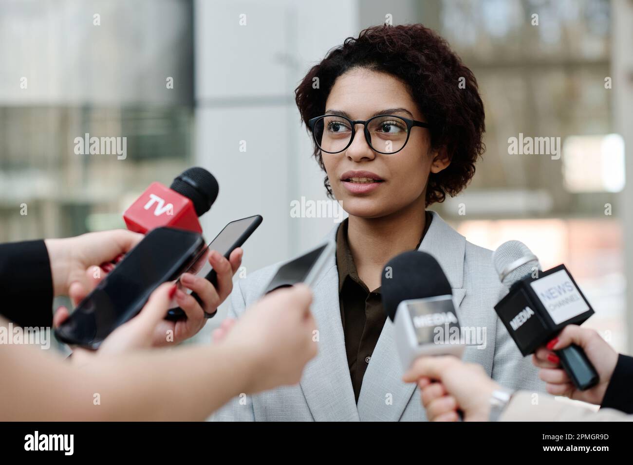 Young businesswoman in eyeglasses giving an interview at business ...