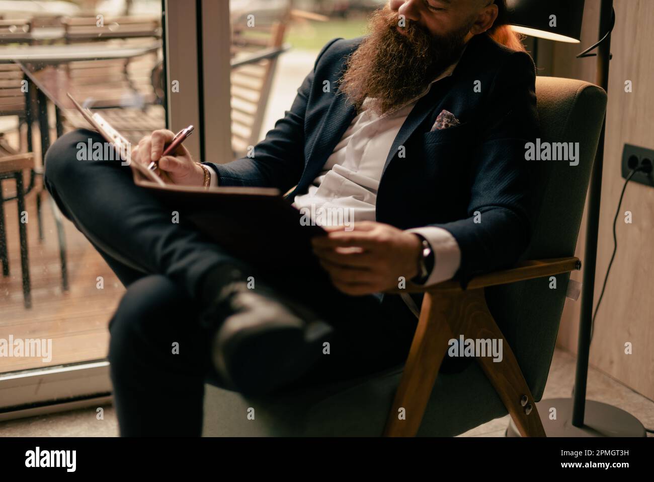Handsome bearded man writing something on his notepad with his legs ...
