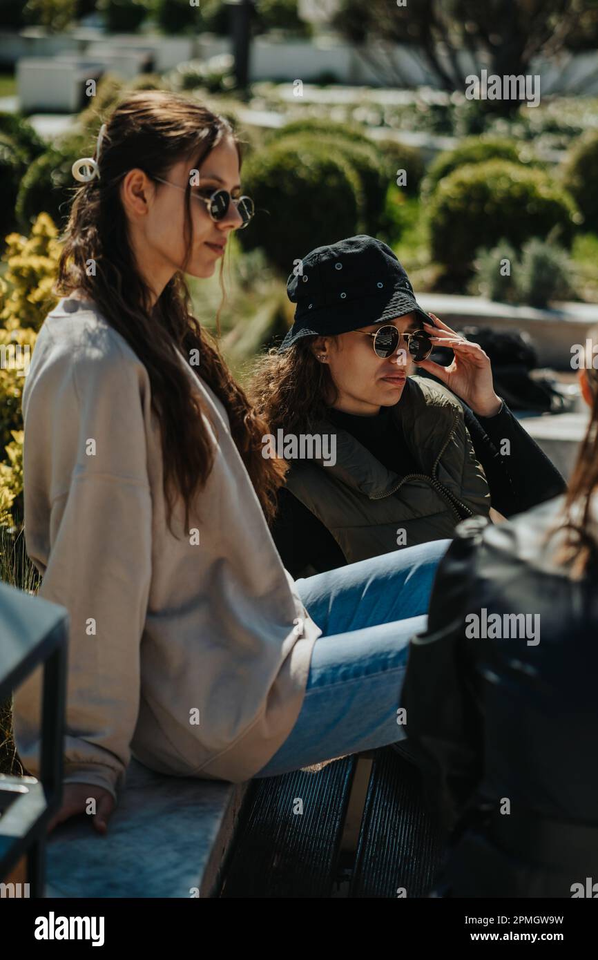 Lovely girls sitting on a bench outside. They are listening to their ...