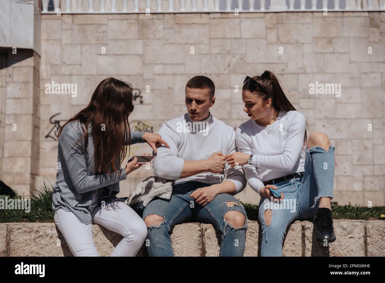 Two brunette girls touching their friend muscles while sitting on the ...