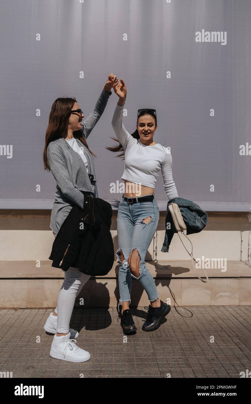Two beautiful girls dancing together in front of the grey wall at the ...