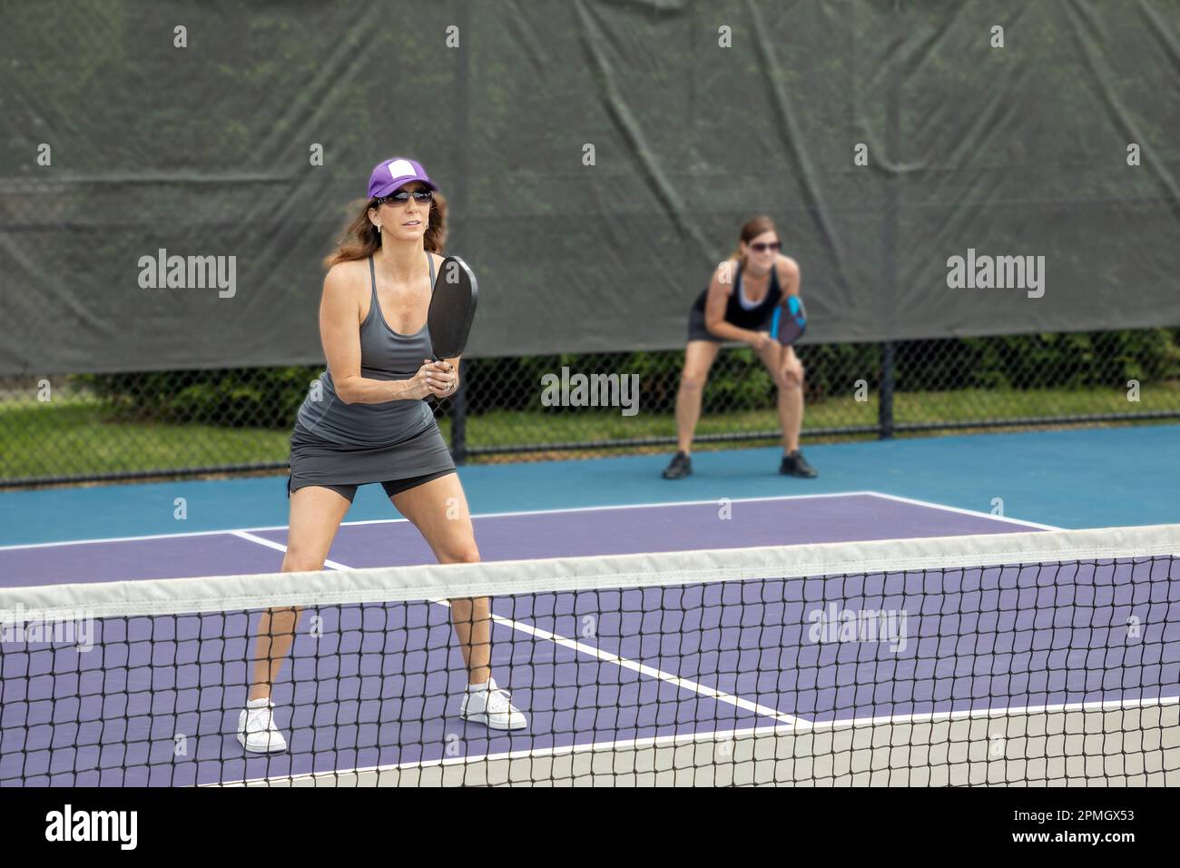 Two pickleball players get ready to return a serve on a court during ...