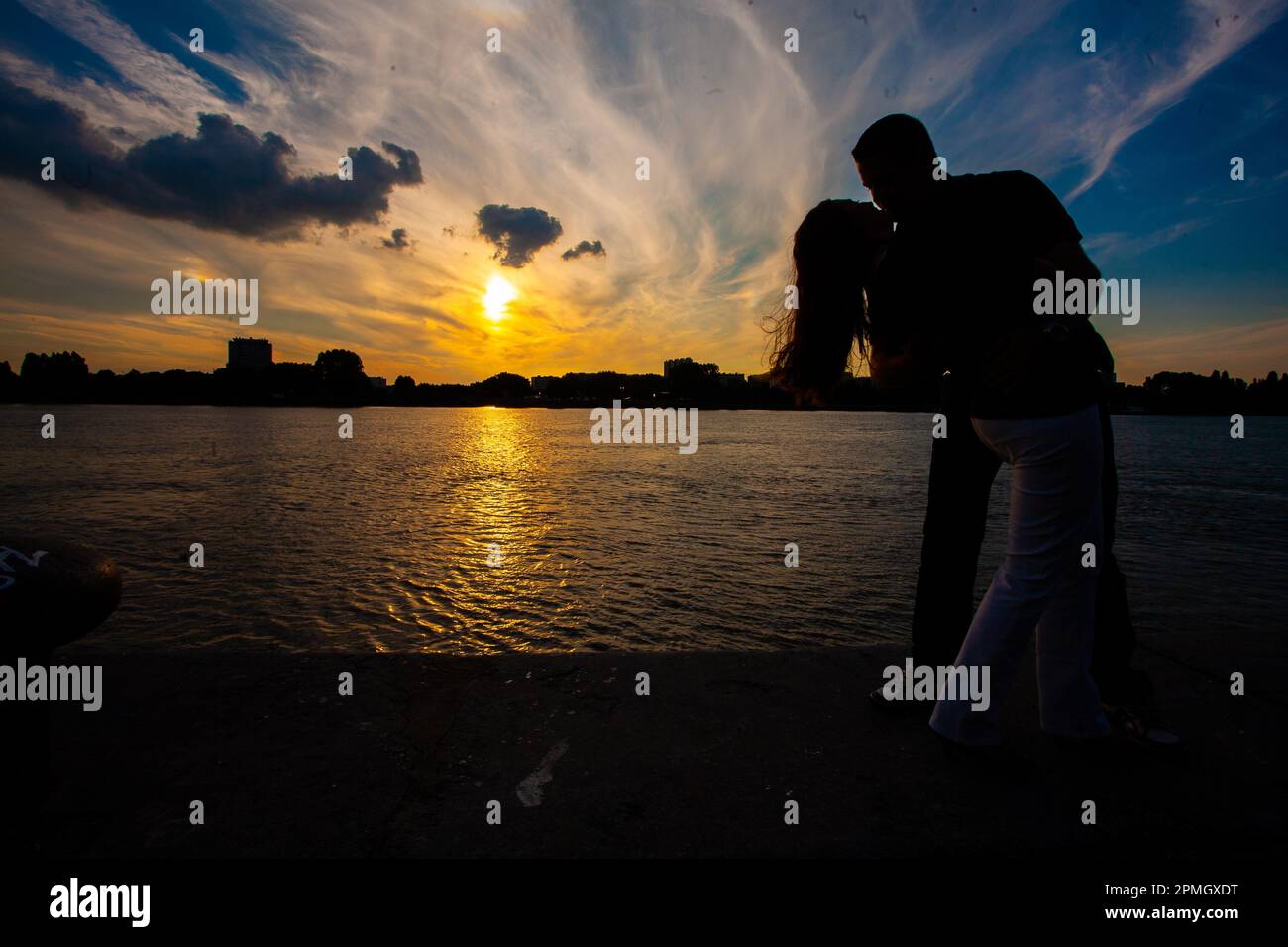 Silhouette of a loving couple cuddling during a golden sunset reflected ...