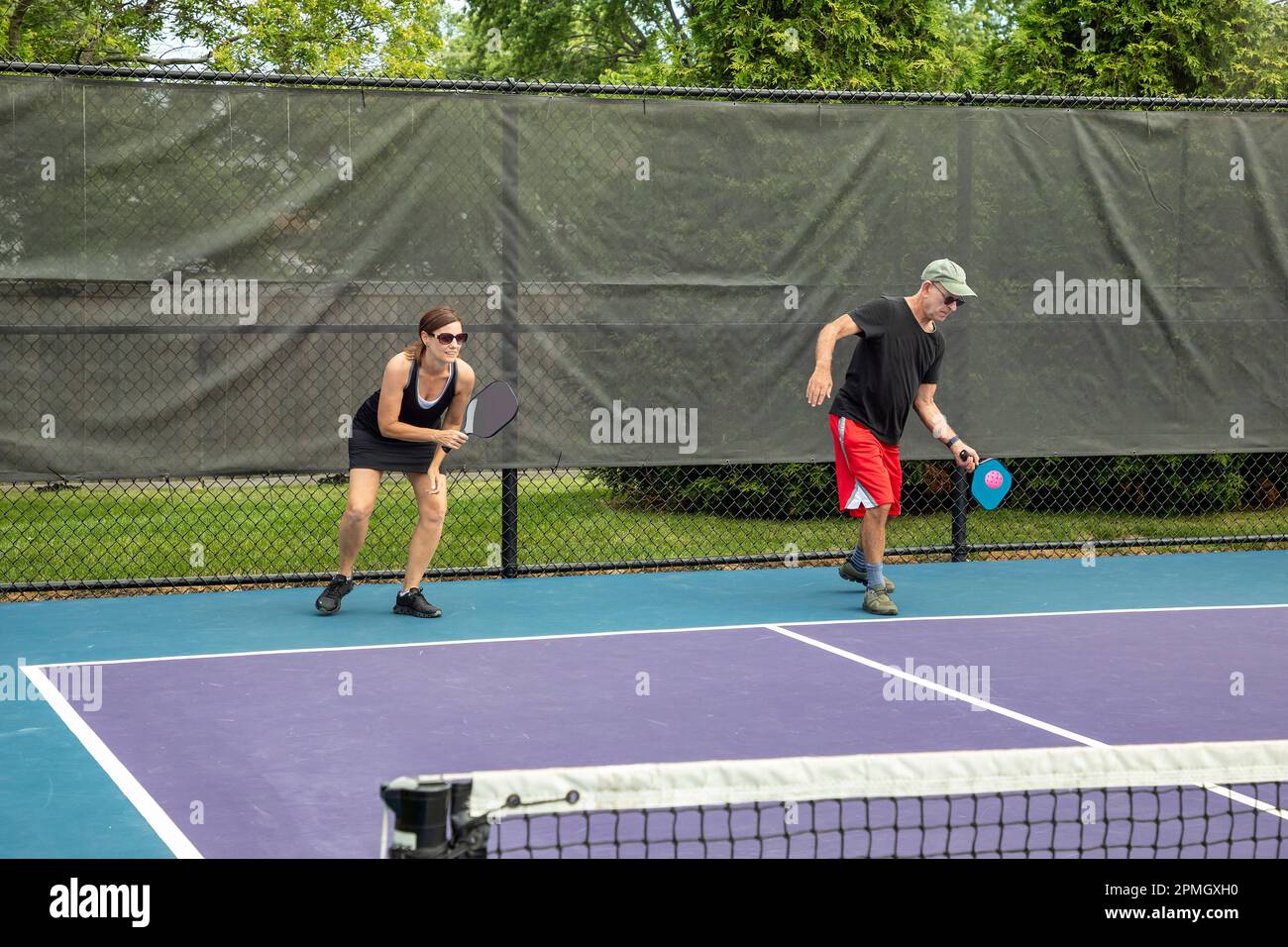 A pickleball player serves while his partner prepares for a return on a ...