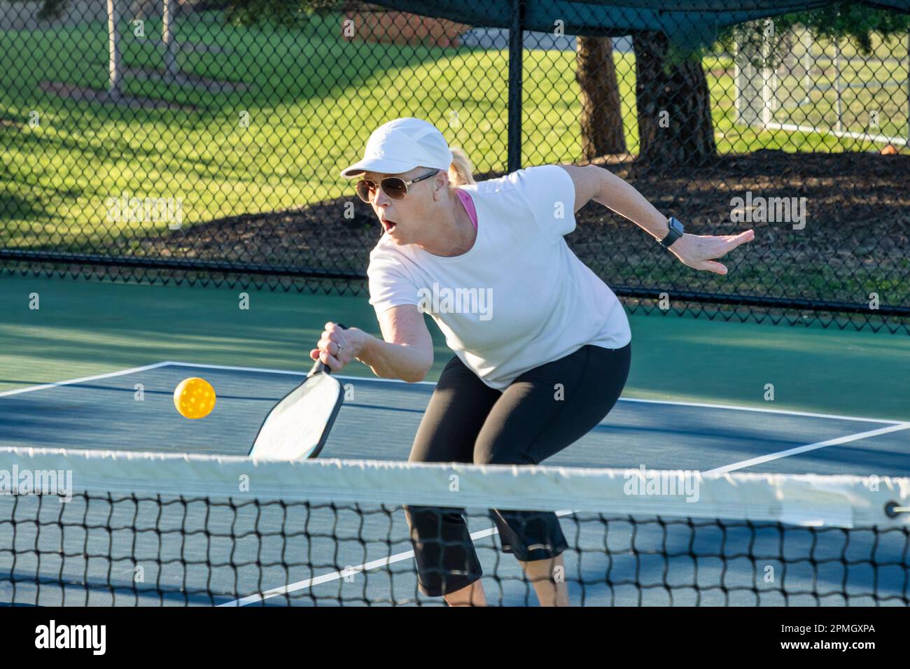 A female pickleball player returns a volley of a bright yellow ball at ...
