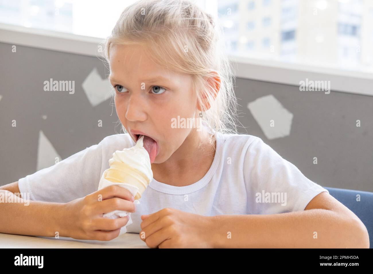 Portrait of a little hungry funny girl eating cold delicious ice cream ...