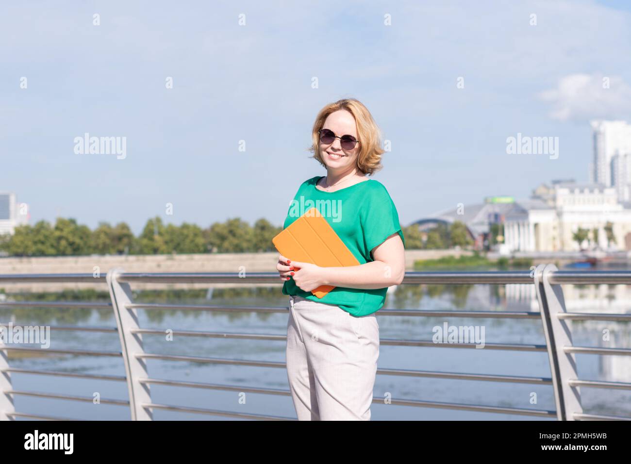 A smiling blogger girl in sunglasses holding a notebook or tablet in ...