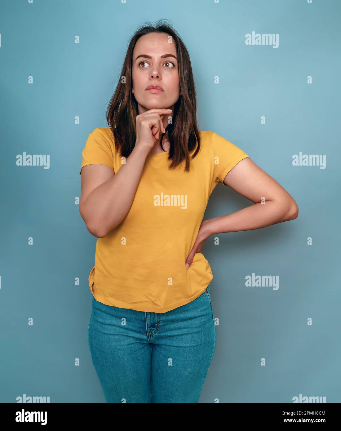 Young lady pondering with her hand on her chin, staring off into ...
