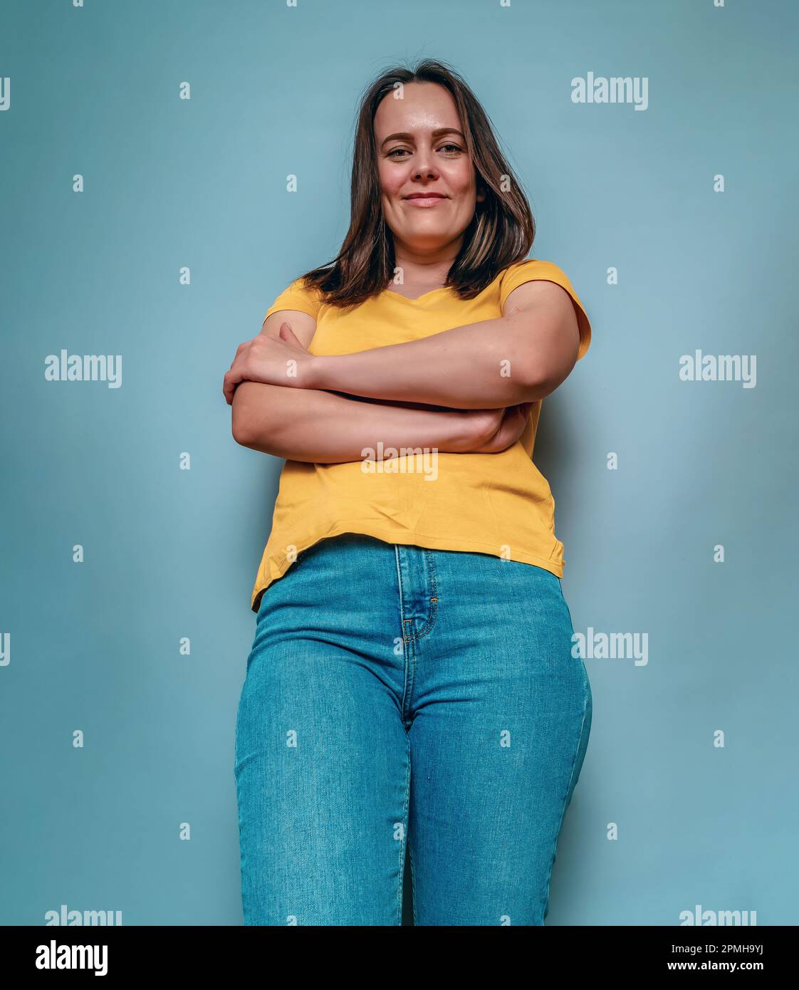 Lower angle young woman crossed arms on blue background Stock Photo - Alamy