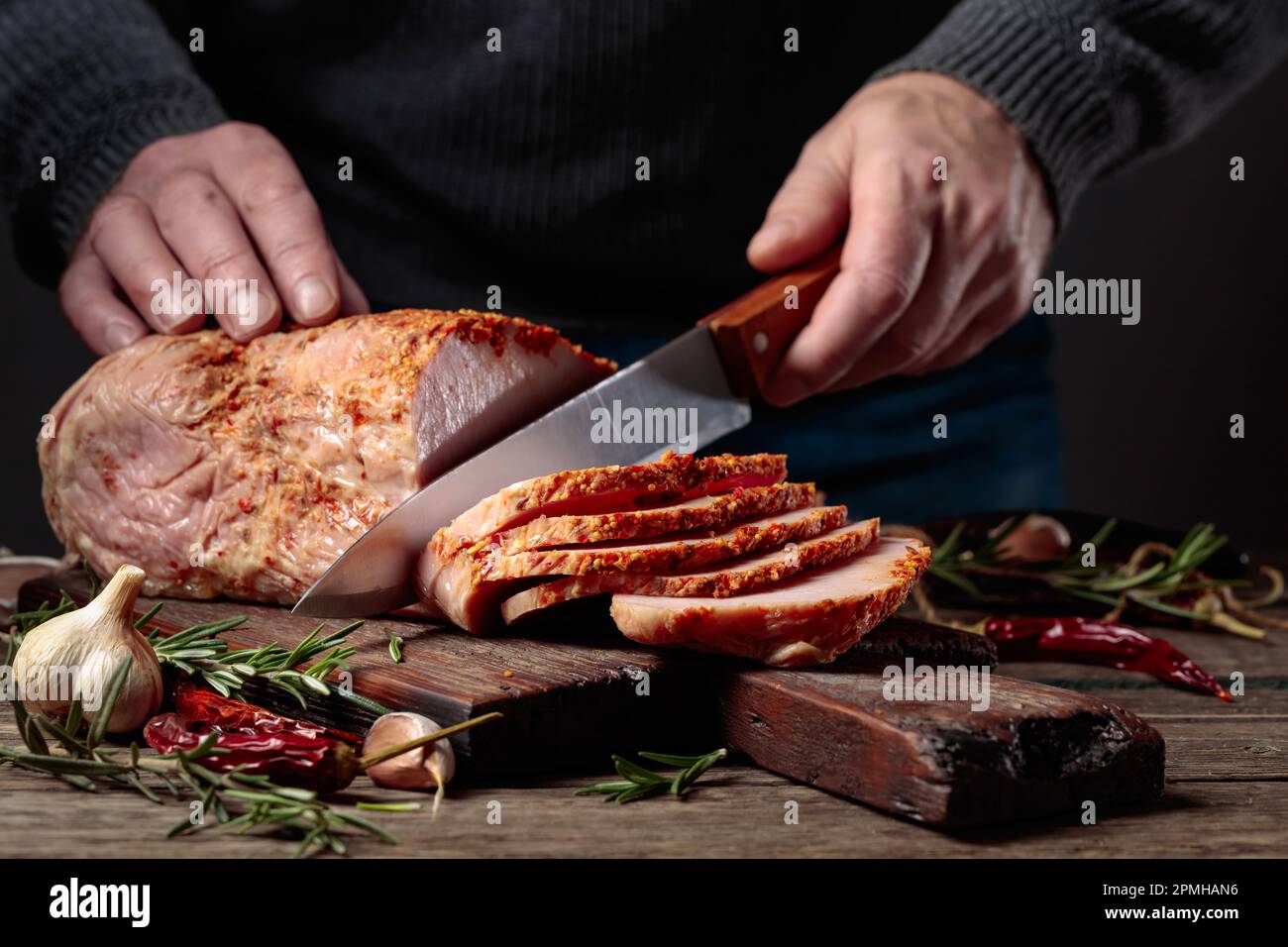 Hands of a male butcher cutting spicy ham on an old wooden table ...