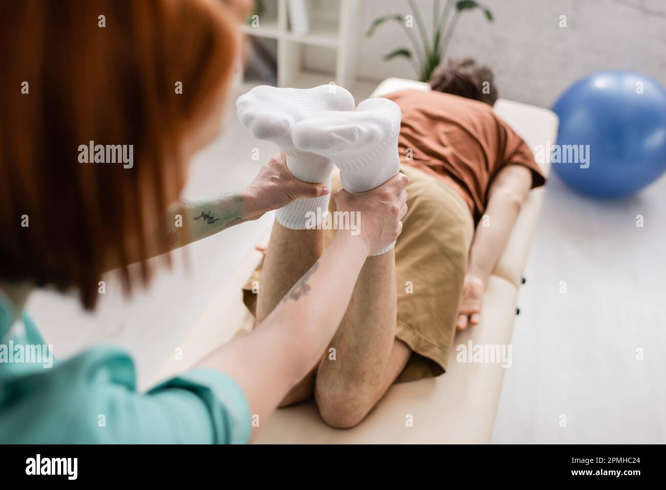 blurred physiotherapist flexing legs of injured man during recovery ...