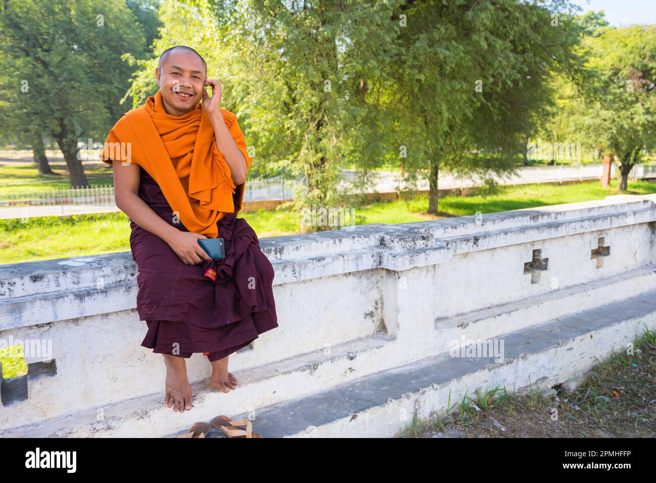 Monk in saffron robe sitting on wall with his cell phone in hand, Royal ...