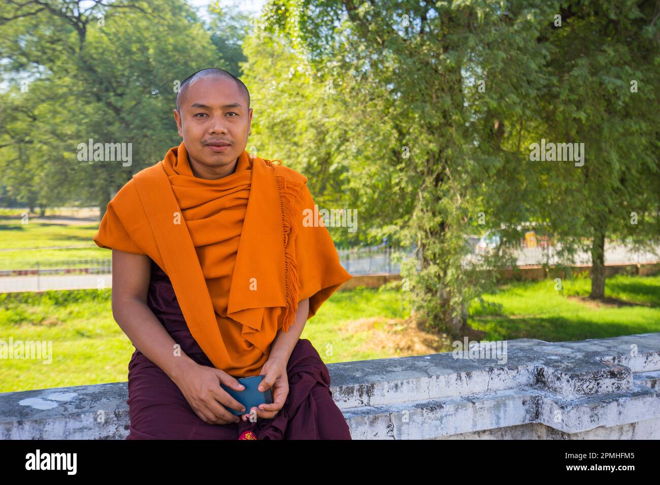 Monk in saffron robe sitting on wall with his cell phone in hand, Royal ...