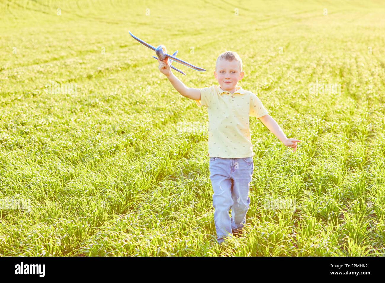 Boy runs with toy airplane in summer through field. Happy child running ...