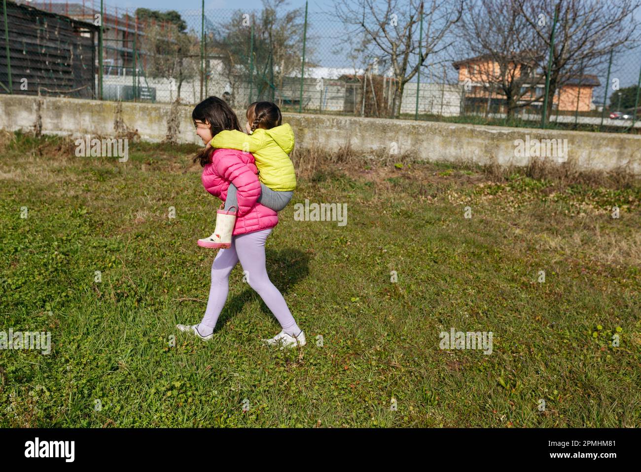 piggyback ride of younger child on elder sister in green field Stock ...