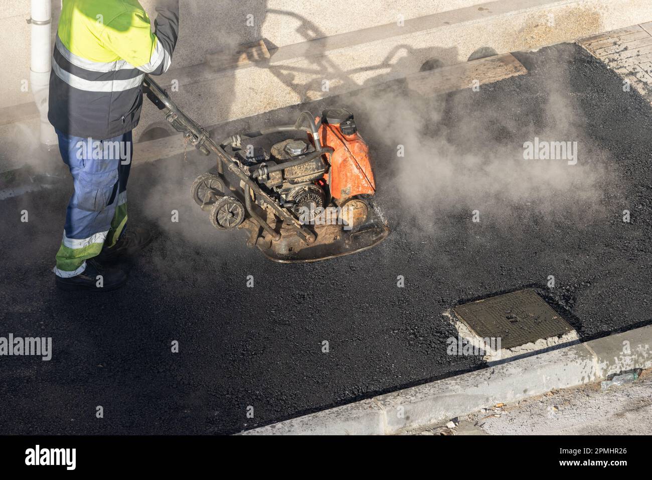 Worker with a vibrating plate compactor machine working on a city ...