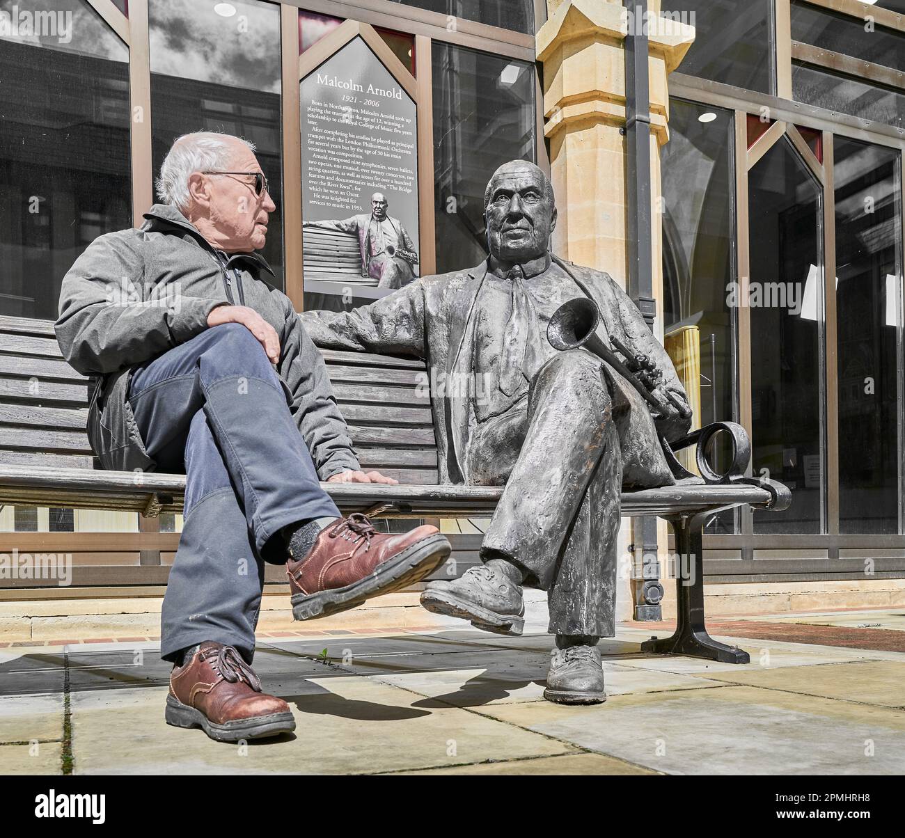 A male senior citizen sits on a bench next to a statue of the famous ...