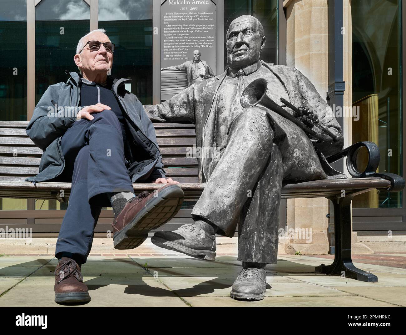 A male senior citizen sits on a bench next to a statue of the famous ...