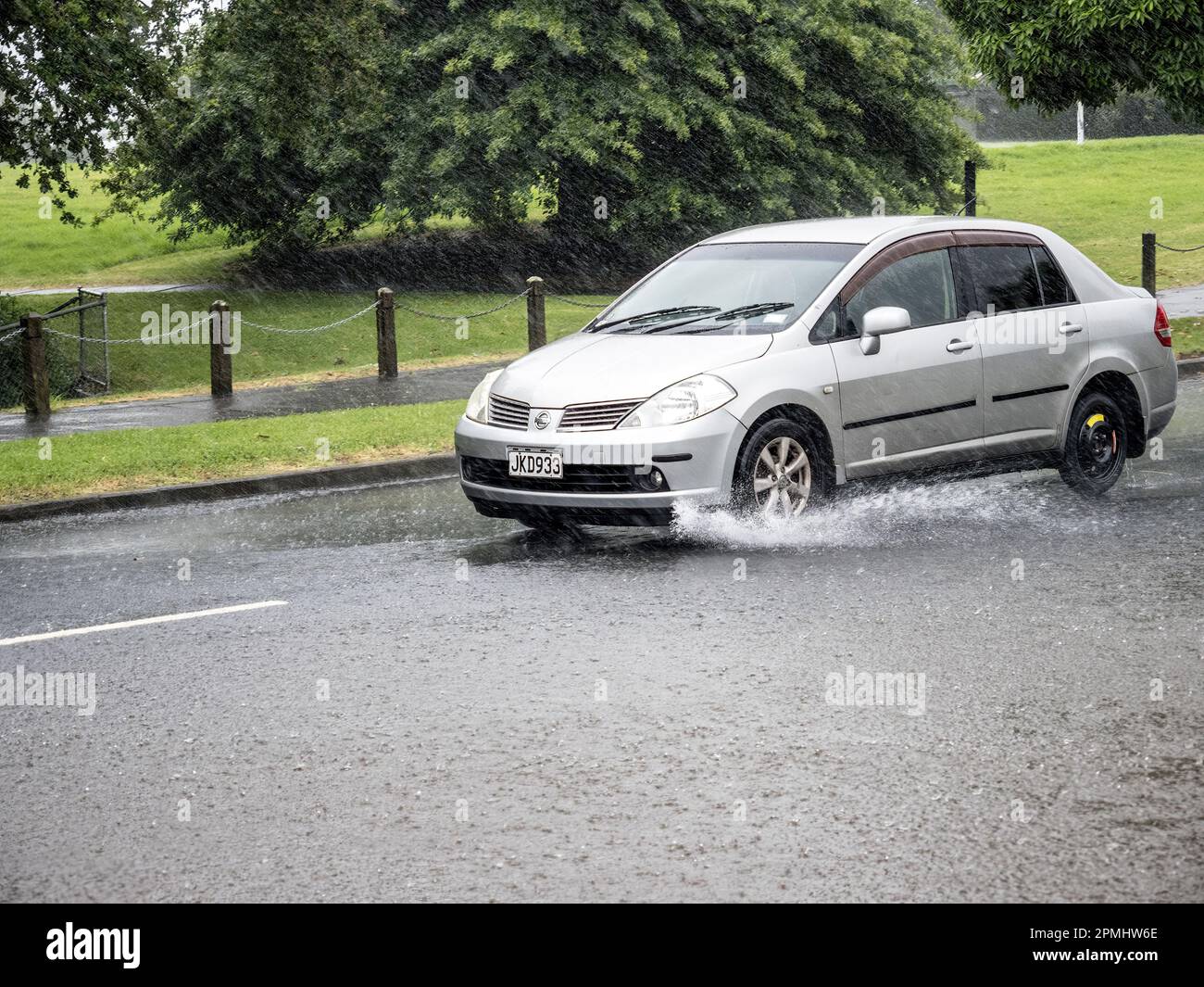 A car driving through a puddle on a wet street next to the sidewalk ...