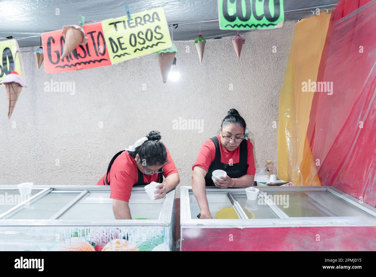 Two Hispanic adult women are serving ice creams on a cup in a street ...
