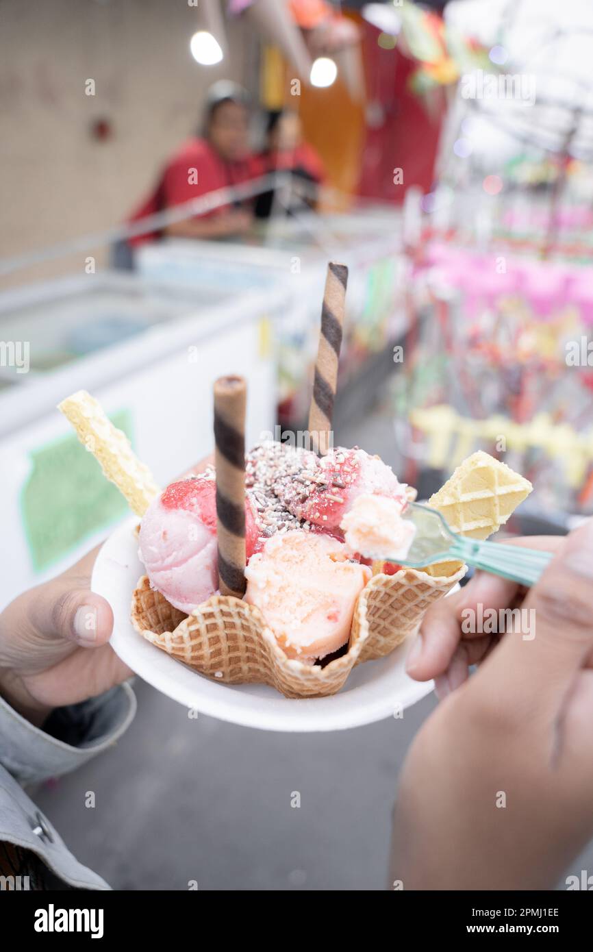 A young Hispanic woman is eating a traditional ice cream in front of a ...